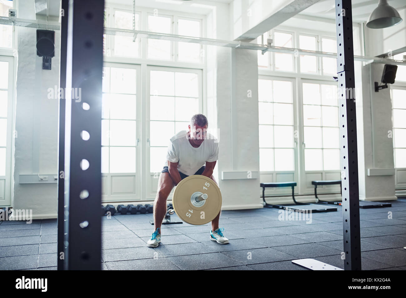 Senior man in sportswear standing alone in a gym focused on lifting ...