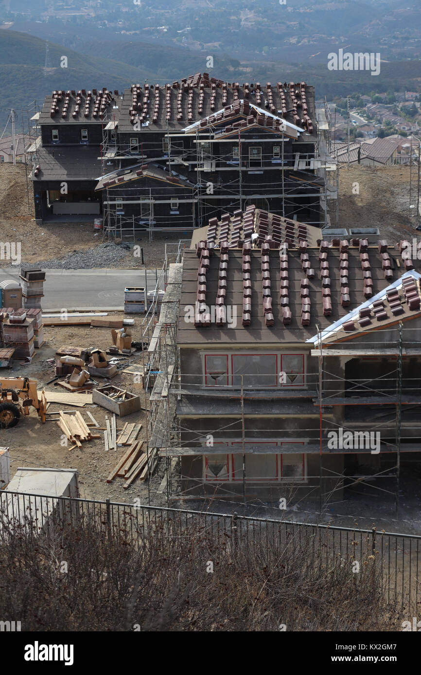Two large new homes under construction with scaffolding, stacked roof ...