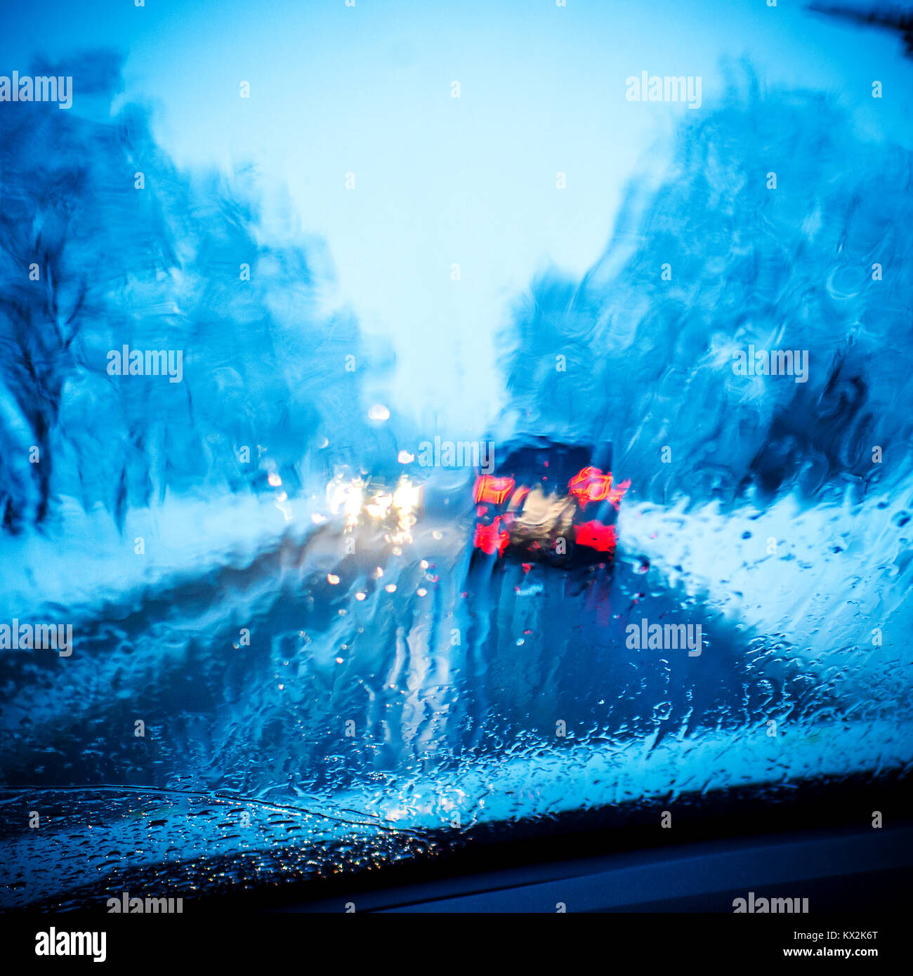 closeup of front car window with raindrops and blurred heavy traffic ...