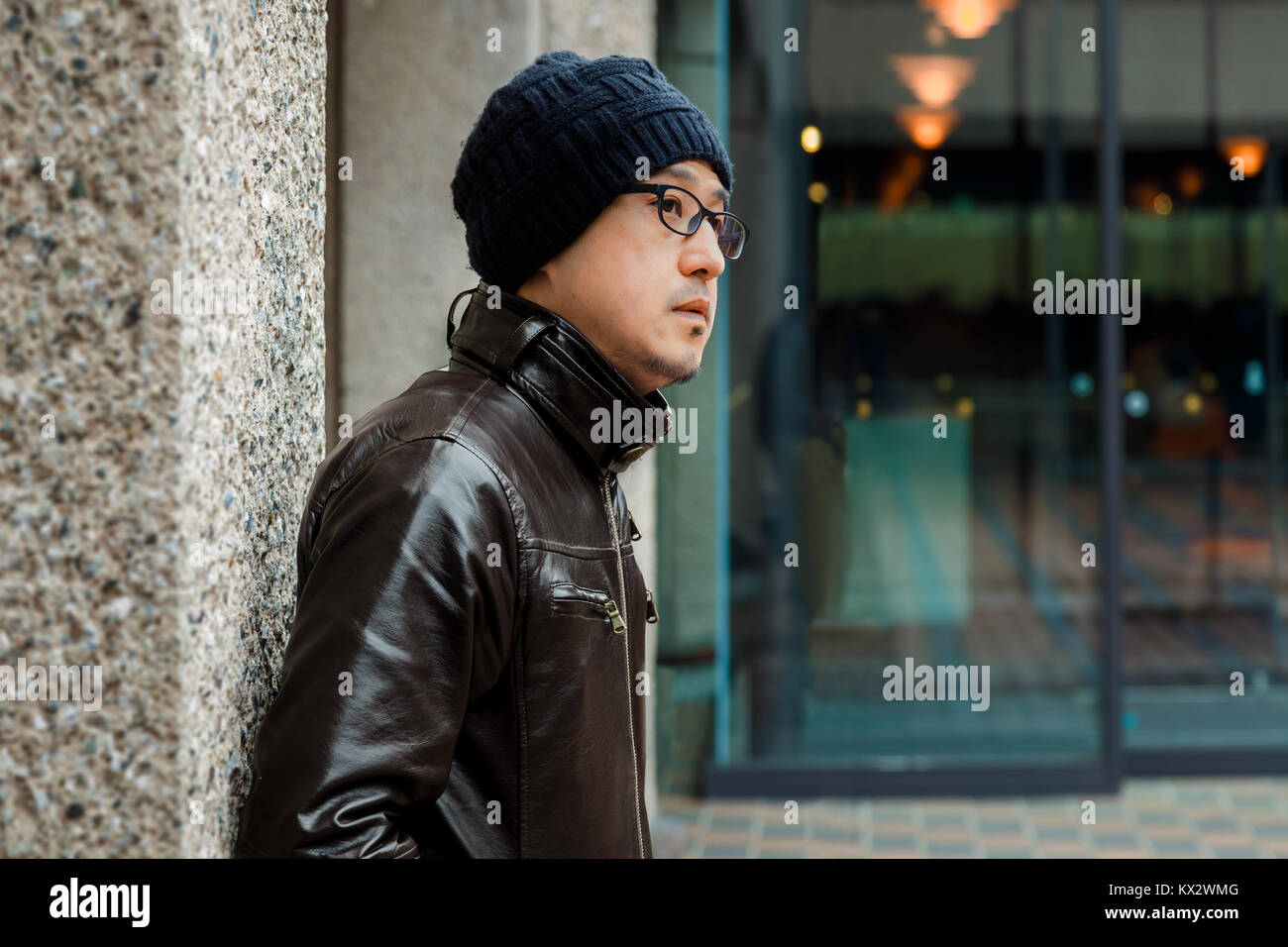 An Asian Man in a Brown Jacket Leans His Back Against the Wall Stock ...