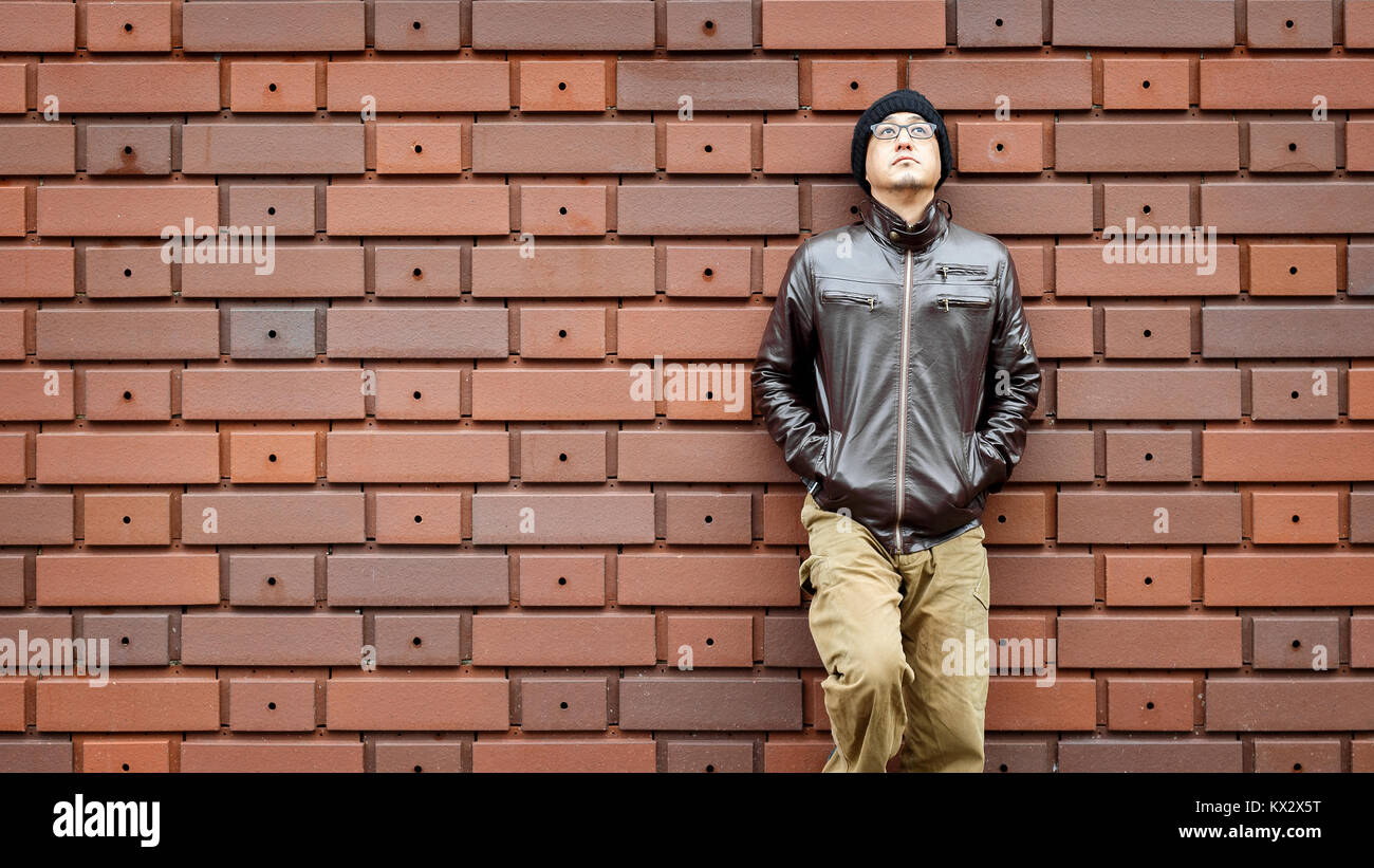 An Asian Man in a Brown Jacket Leans His Back Against the Wall Stock ...