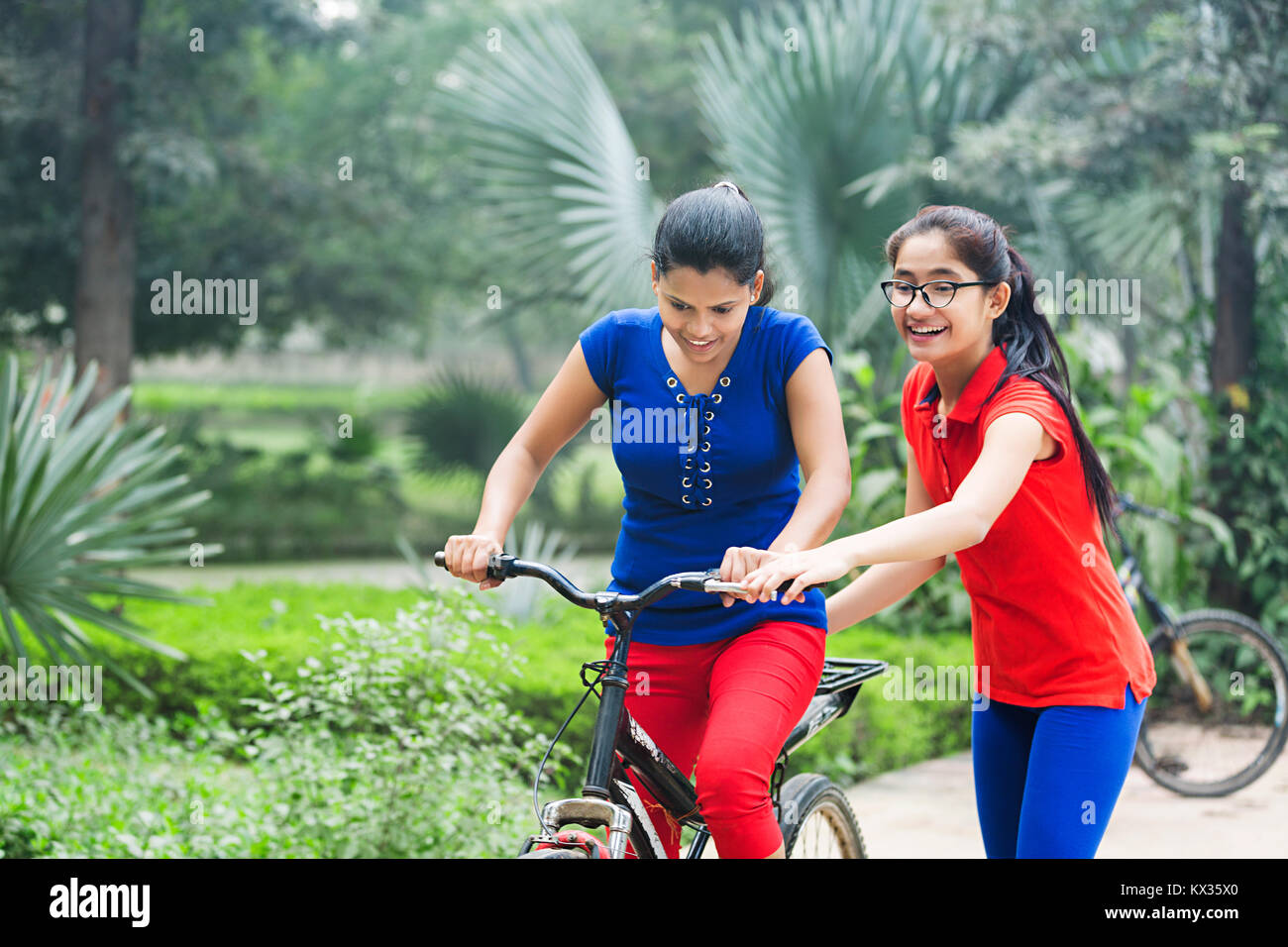 Young Girls Riding Bicycle Friend Helping Support Park Stock Photo - Alamy