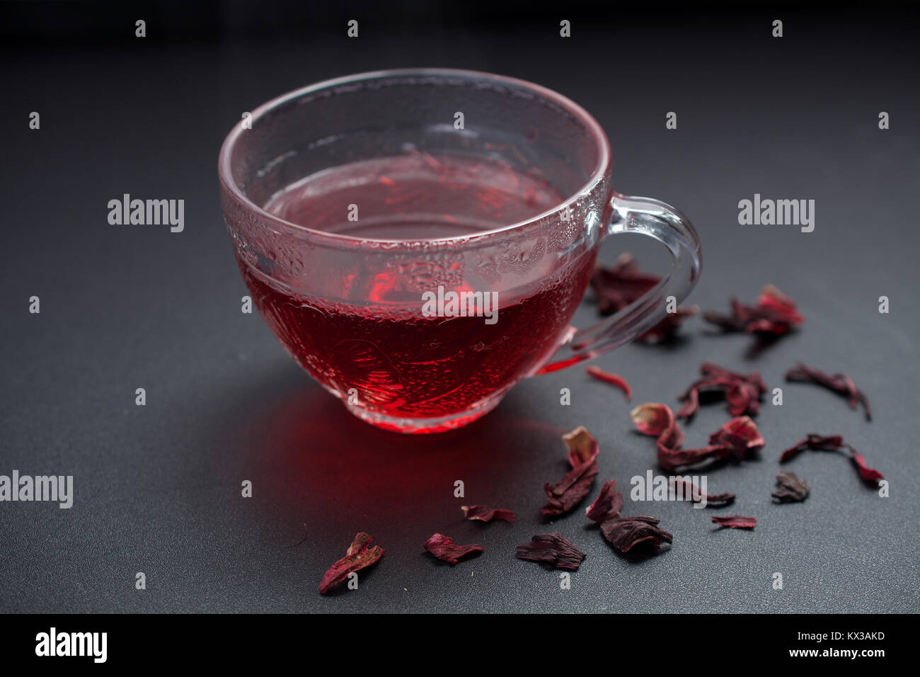 Red hibiscus tea in transparent cup on black table decorated with dried ...
