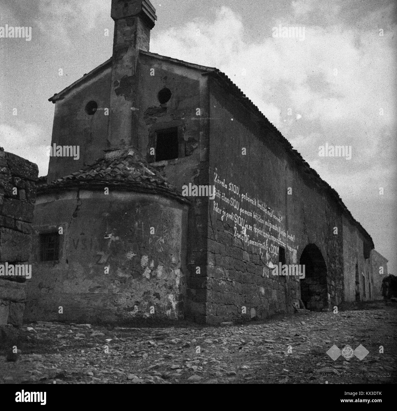 A 1950 photograph depicts two houses in Lopar joined by an arch ...