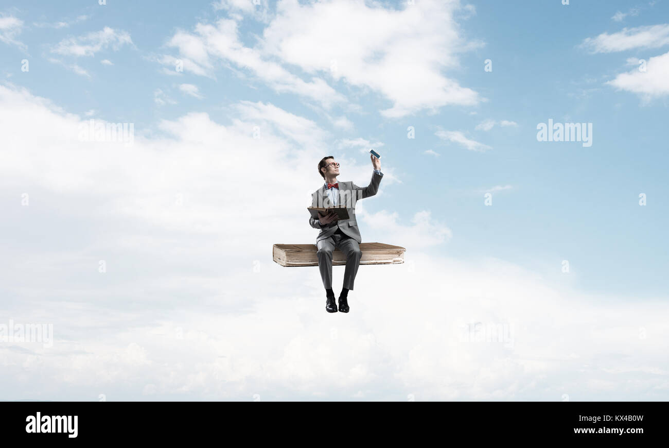 Young businessman or student floating in blue sky and studying the ...