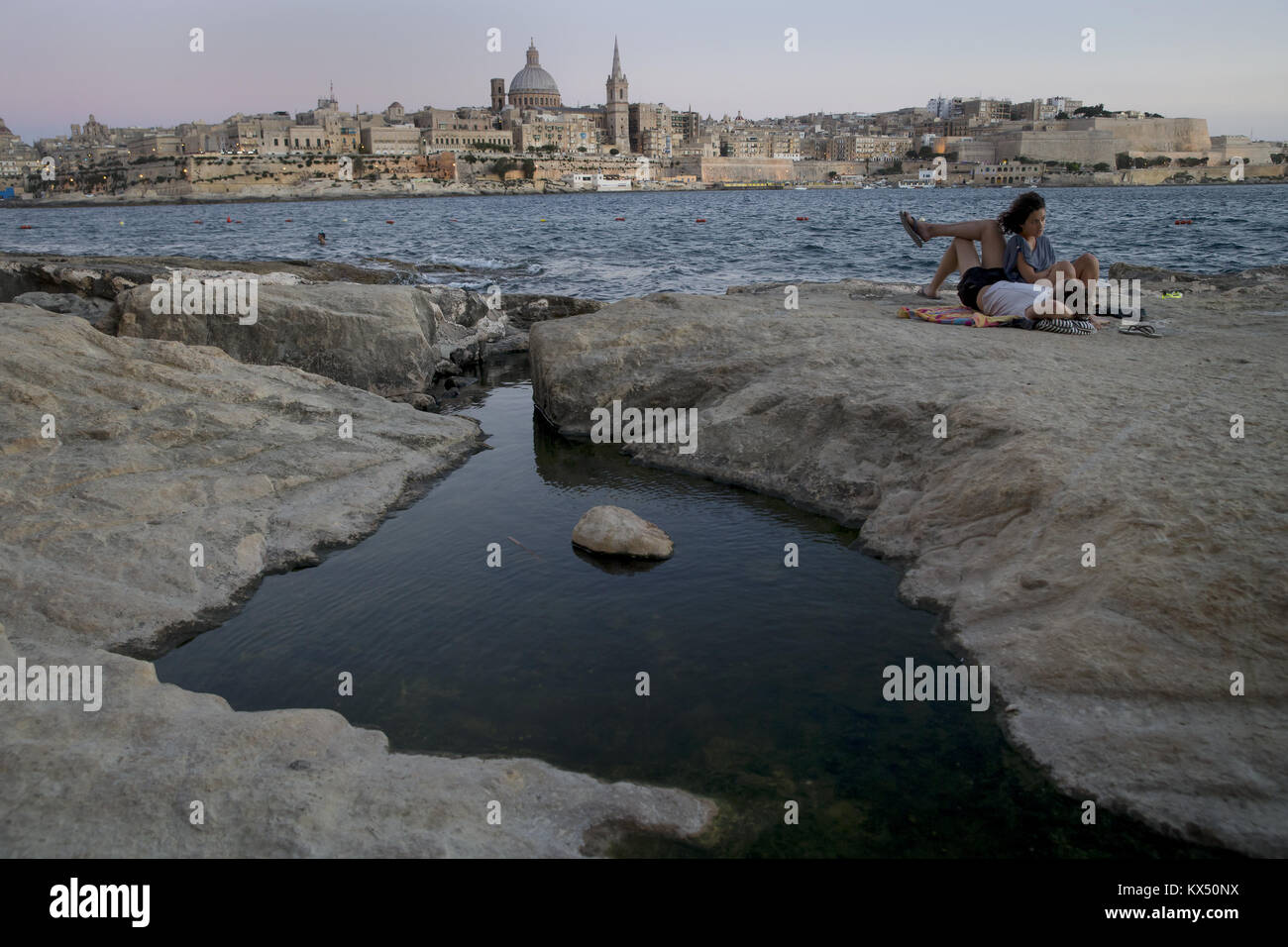 People enjoying the rocky beach at Sliema, with the Marsamxett Harbour ...