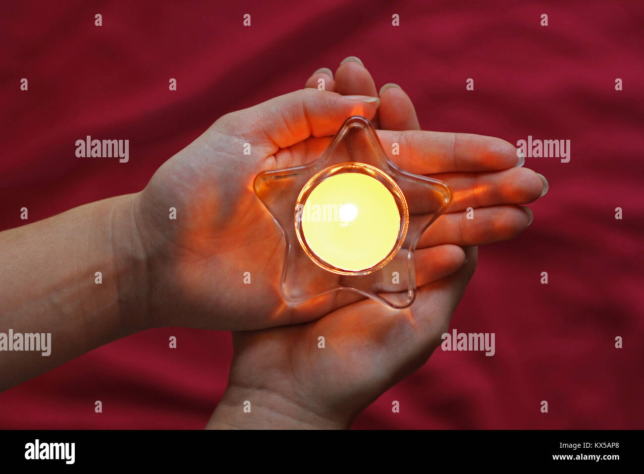 hands of a woman holding a lit tea light in star shape, top view, red ...
