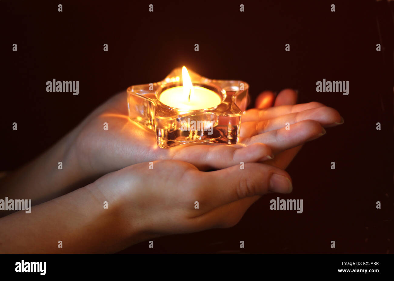 hands of a woman holding a lit tea light in star shape, low key, dark ...