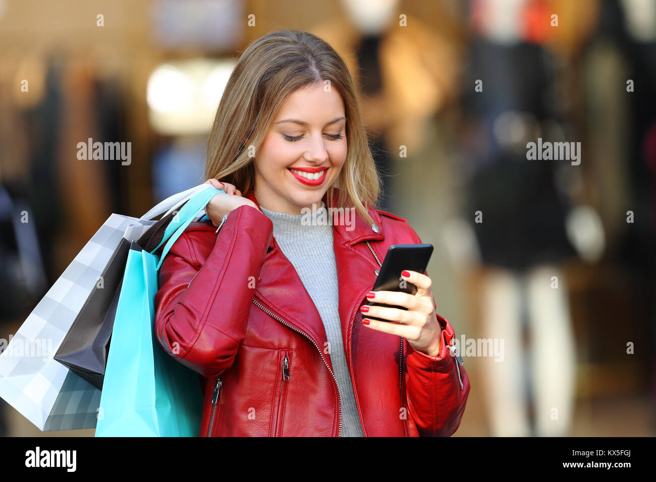 Portrait of a happy shopper holding shopping bags using a smart phone ...