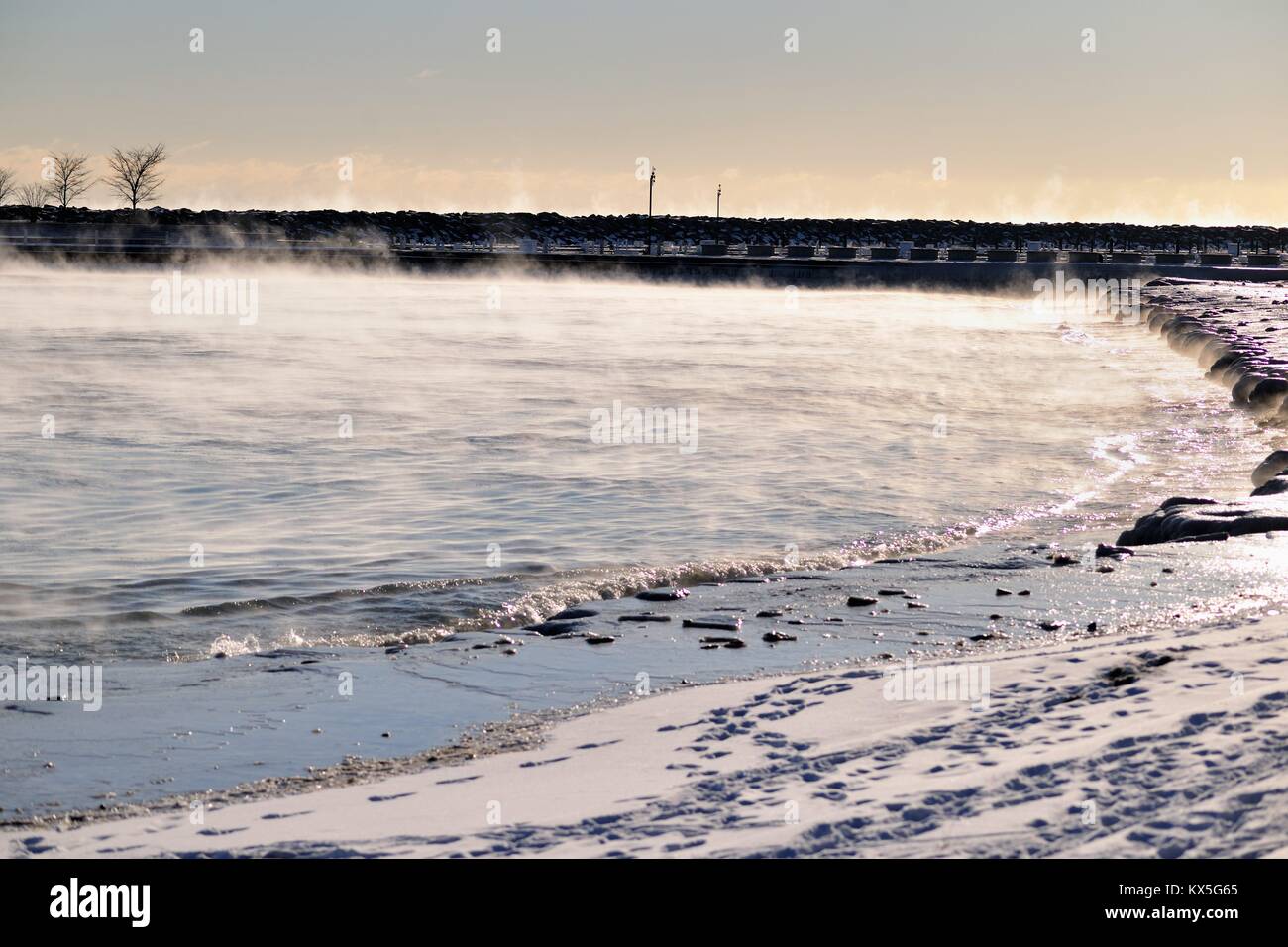 Vapor rises from still flowing water as turns to Ice on Lake Michigan ...