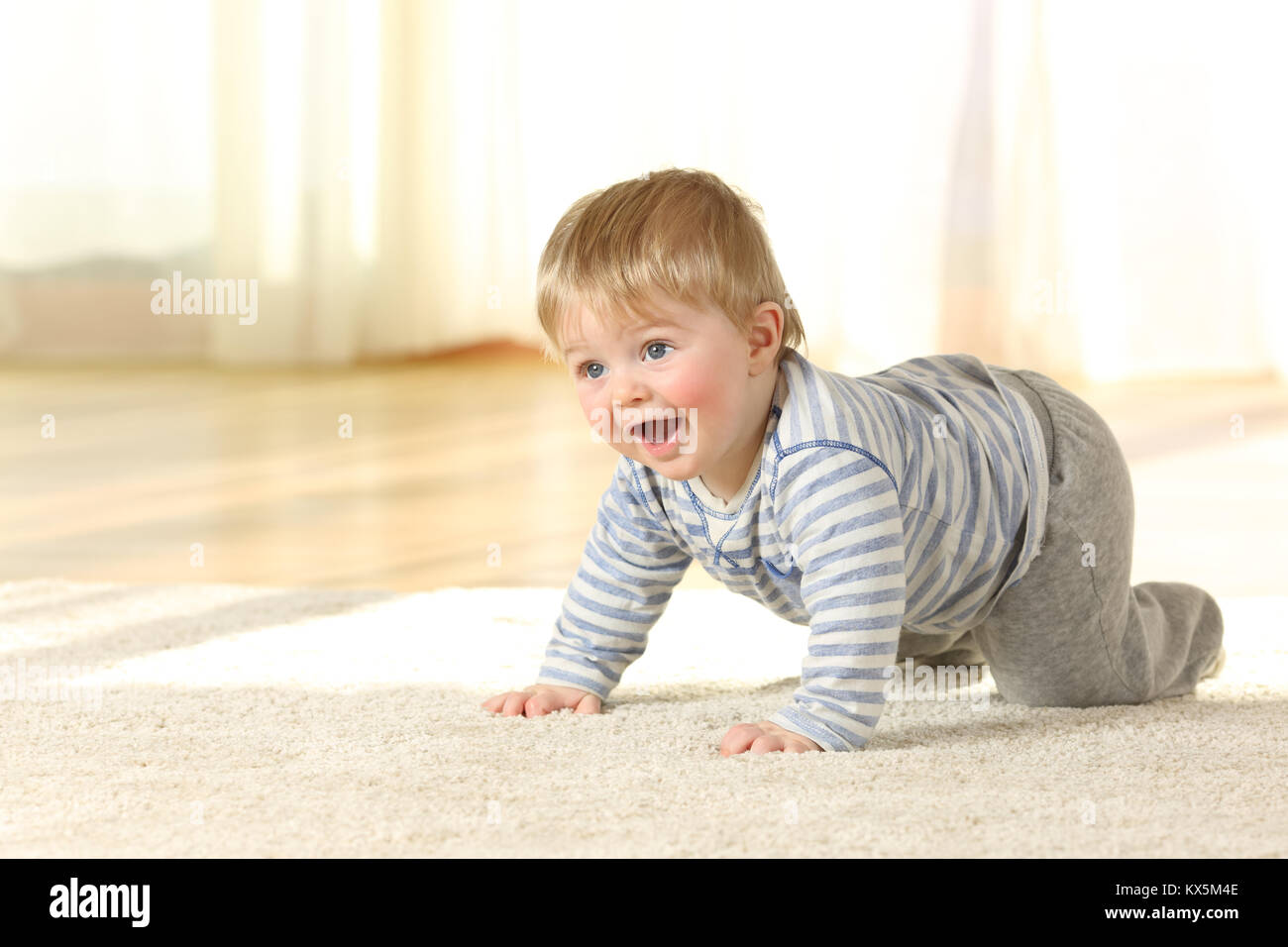 Happy baby crawling and laughing on a carpet at home with a warm light ...