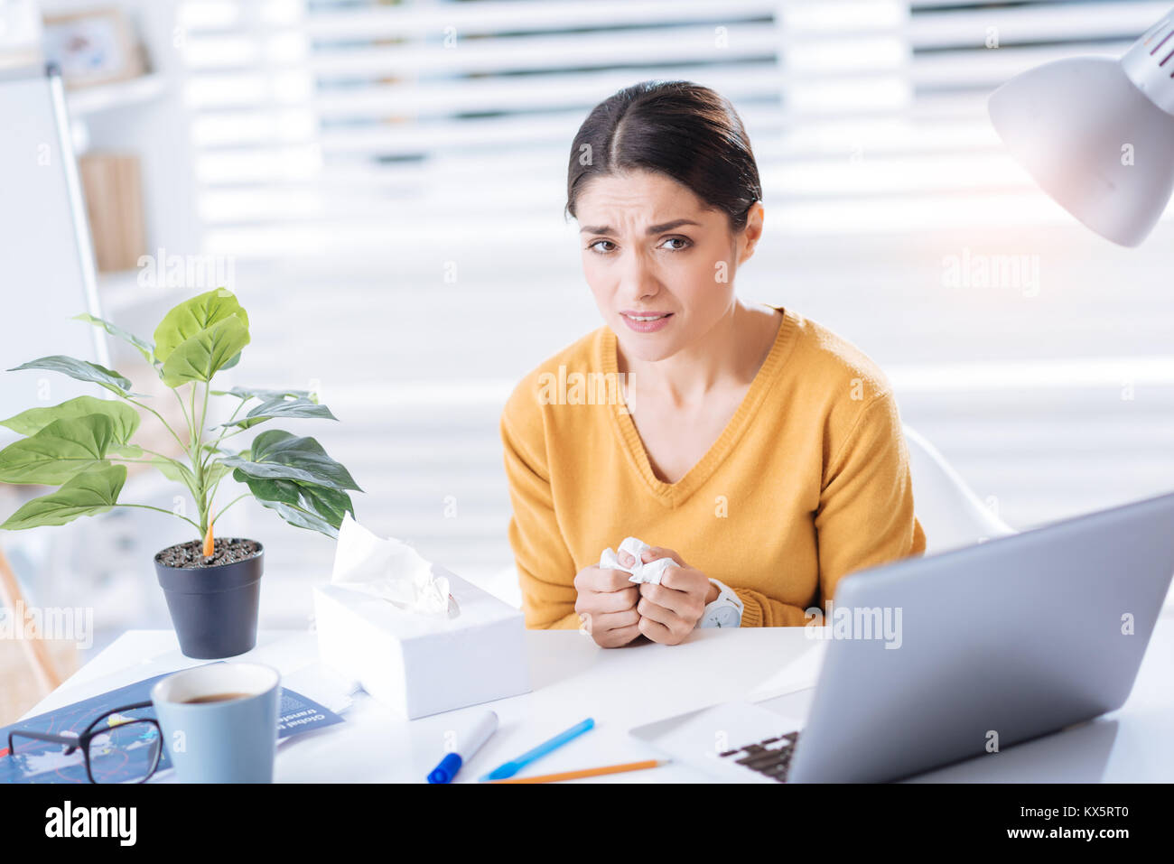 Ill woman frowning while sitting at her working place and constantly ...