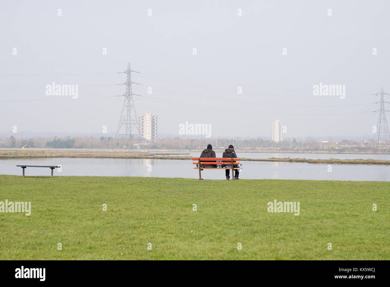 Two people sitting on a bench looking at Electrical pylon and hi-rise ...