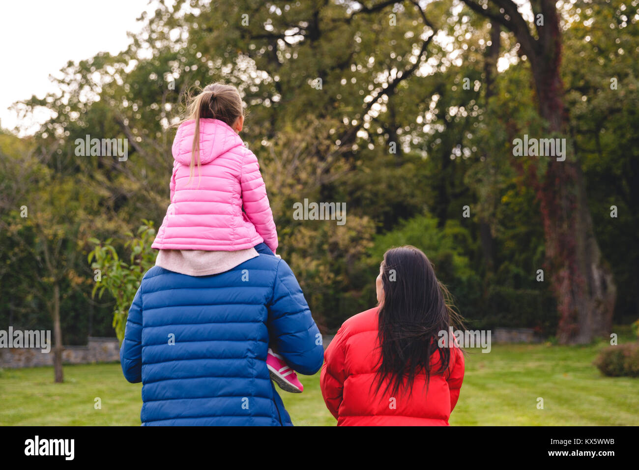 Back view of a young family spending time together outdoors, dad giving ...