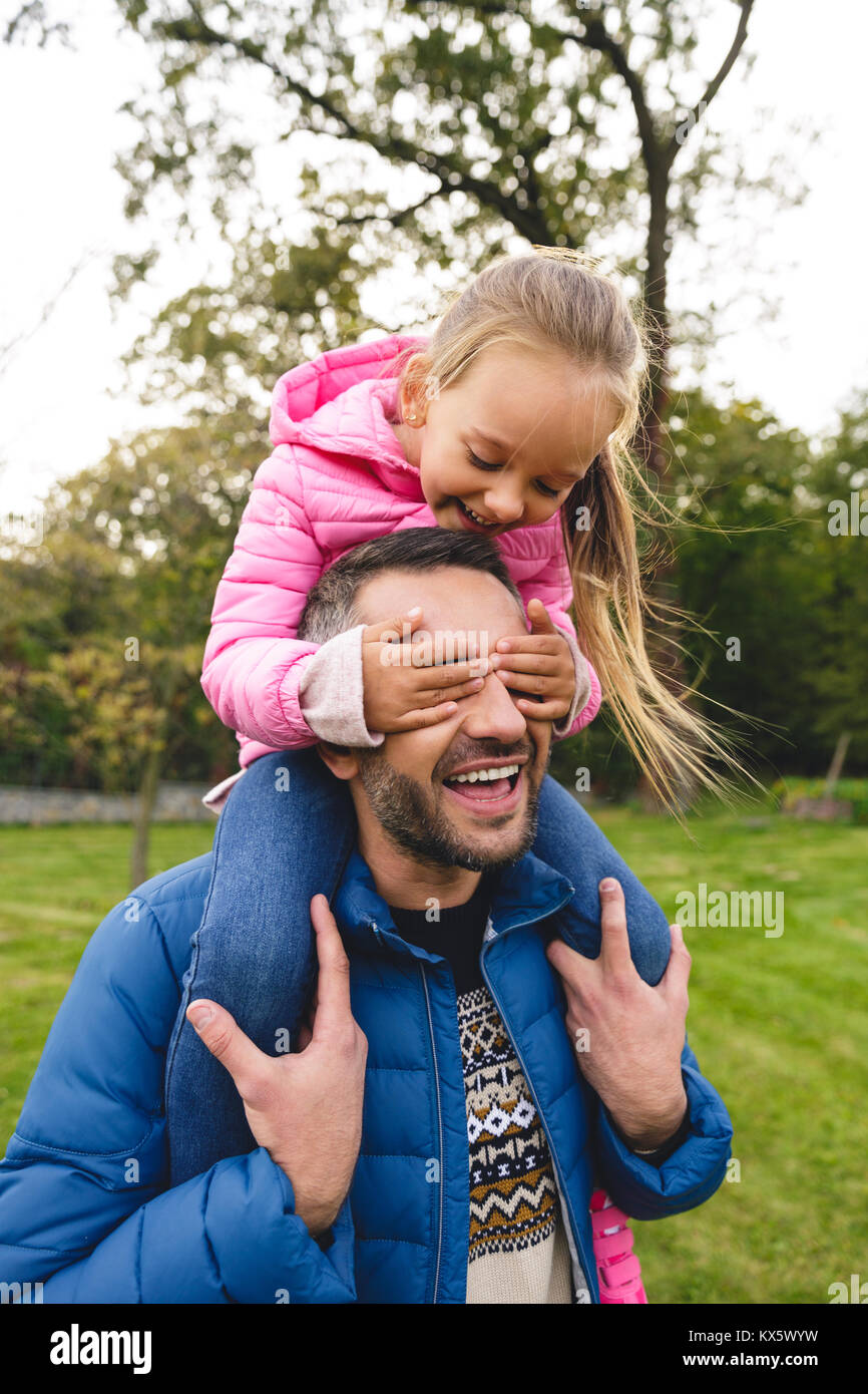 Smiling little girl riding on father's back in the park, girl covers ...