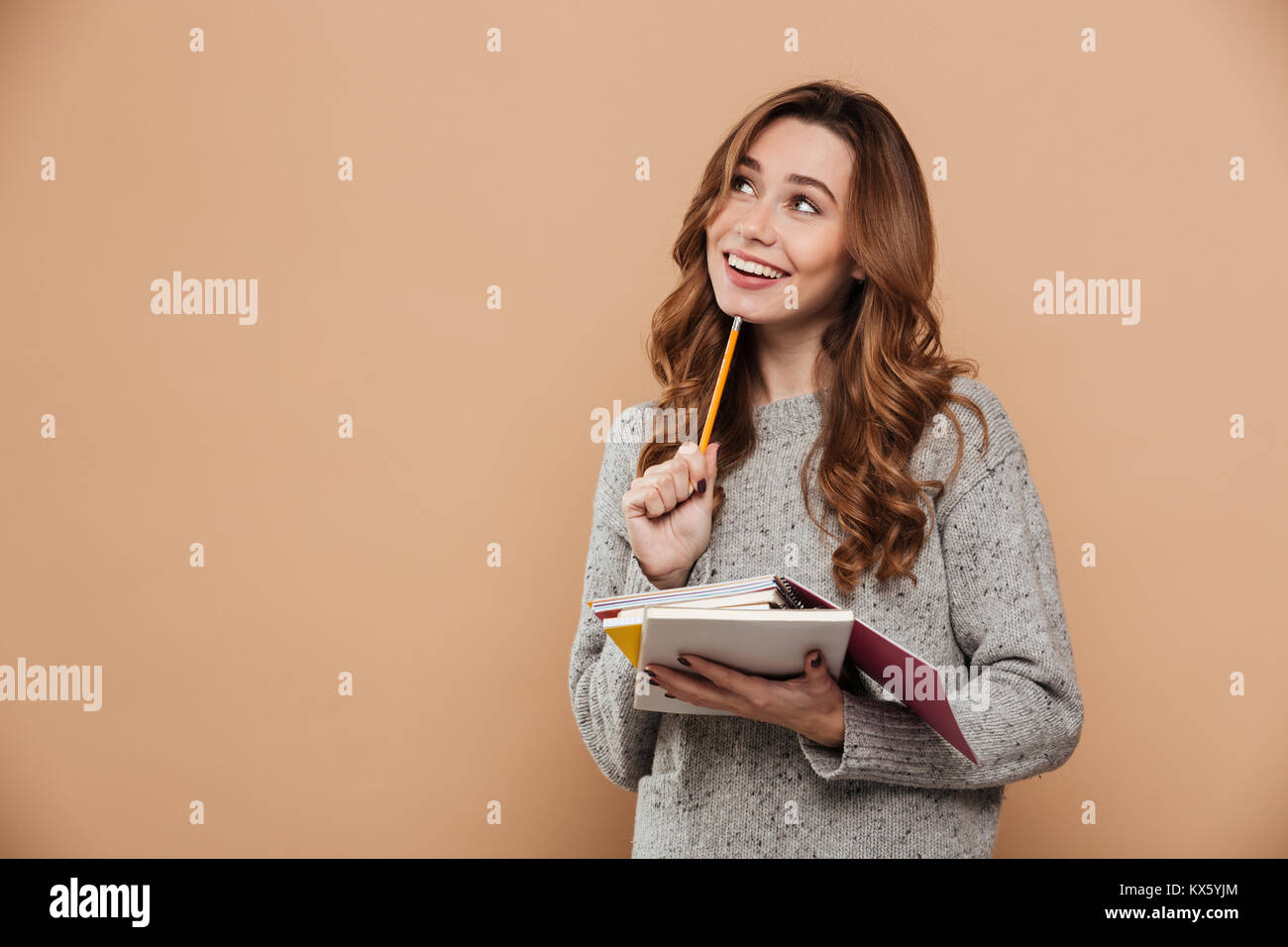 Portrait of happy thinking female student in warm sweater holding ...