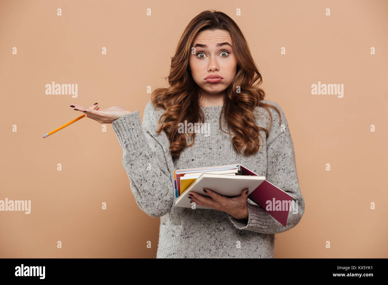 Portrait of pretty confused female student holding notebooks and ...