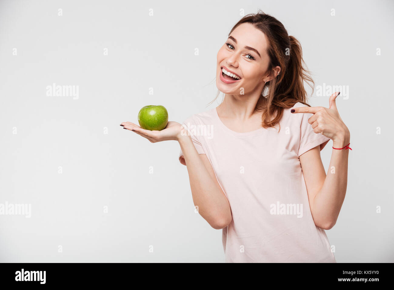 Portrait of a smiling pretty girl holding an apple and pointing finger ...