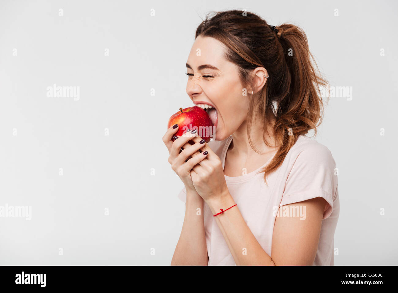 Close up portrait of a hungry pretty girl biting an apple isolated over ...