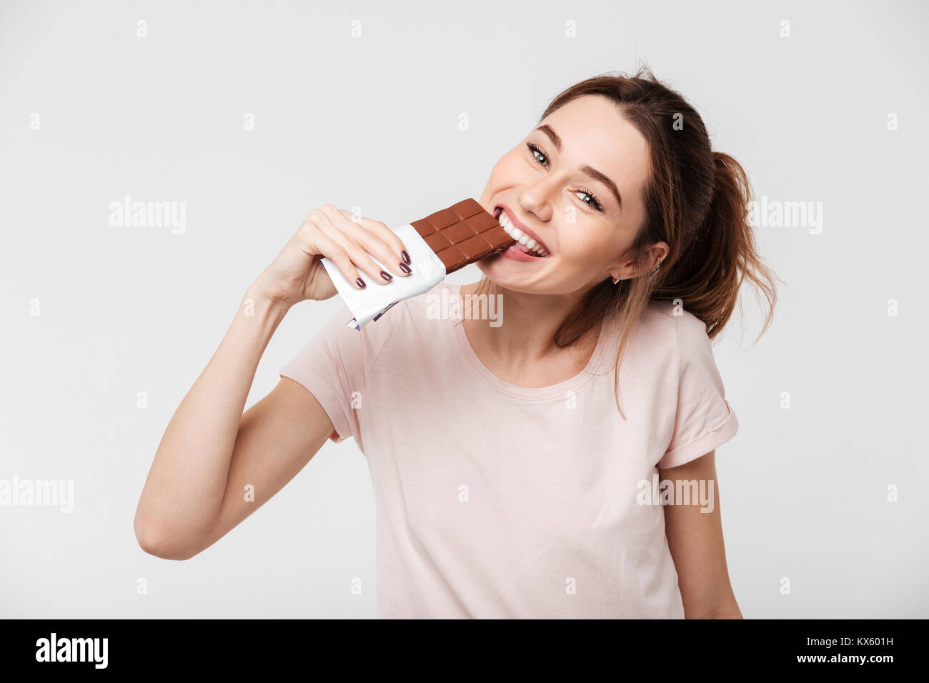 Portrait of a smiling pretty girl biting chocolate bar and looking at ...