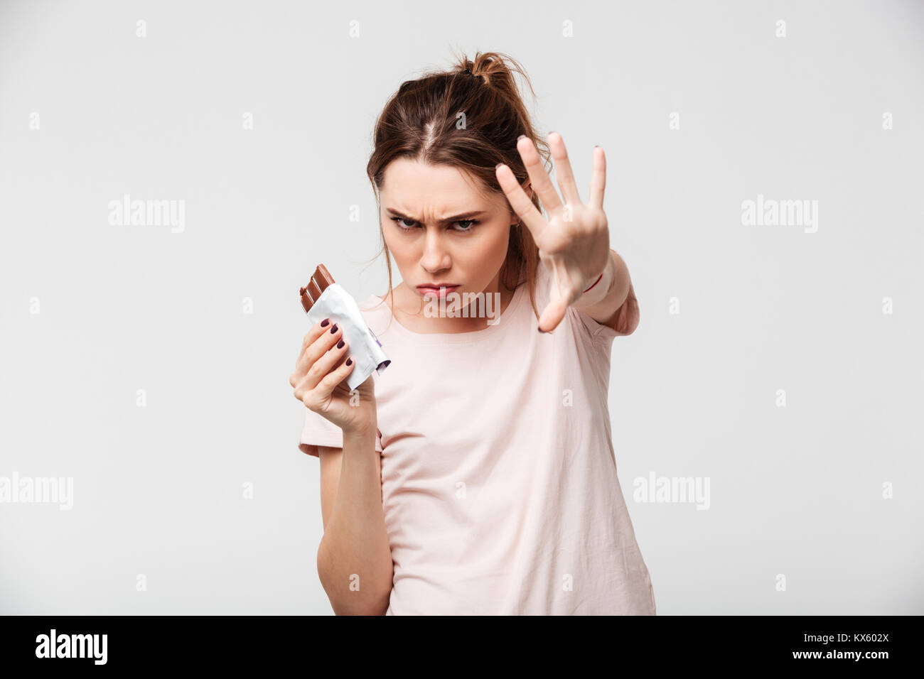 Portrait of an angry cute girl holding chocolate bar and showing stop ...