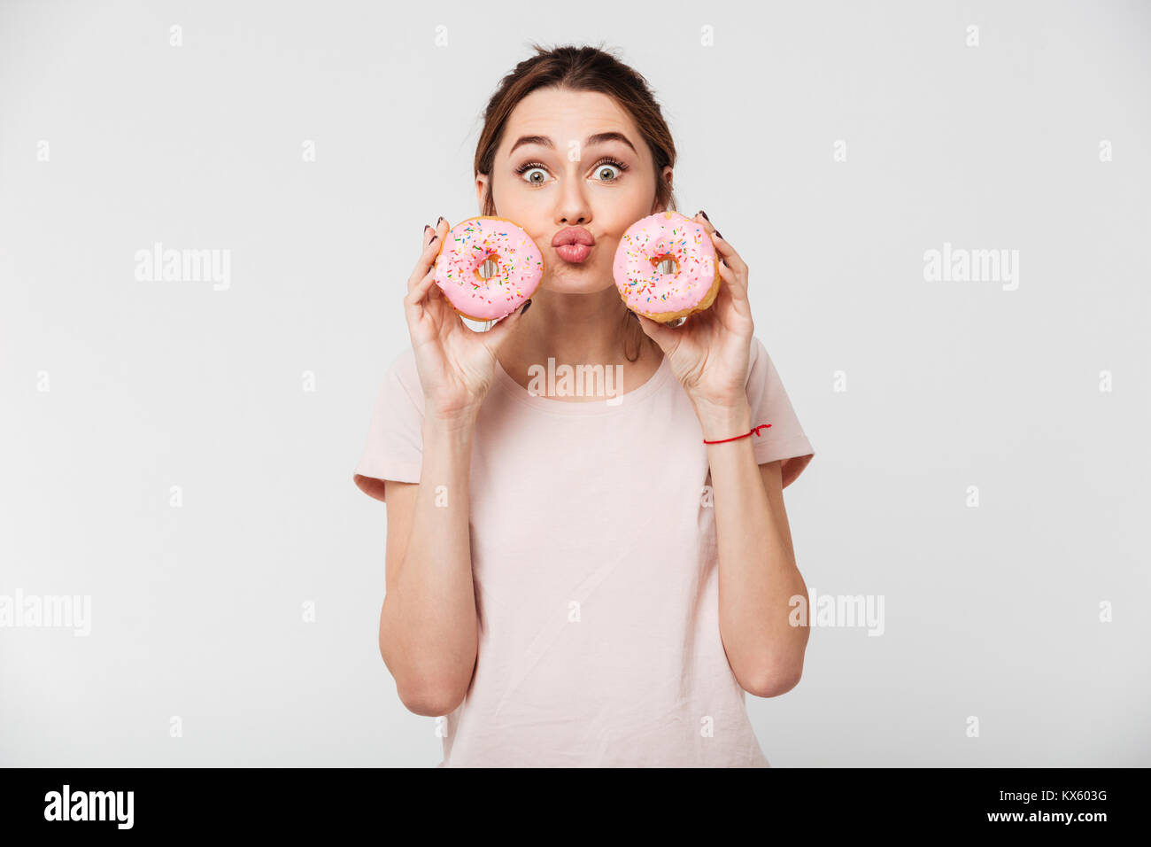Portrait of a cheery pretty girl holding donuts at her face isolated ...