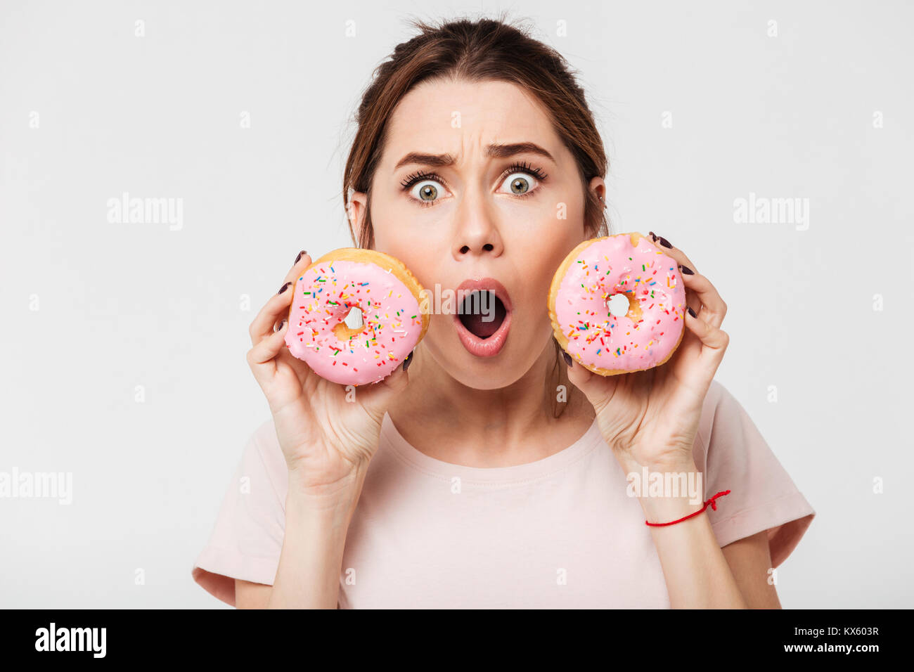 Close up portrait of a shocked pretty girl holding donuts at her face ...