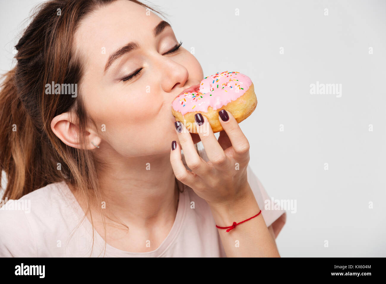Close up portrait of a pleased pretty girl eating donuts isolated over ...