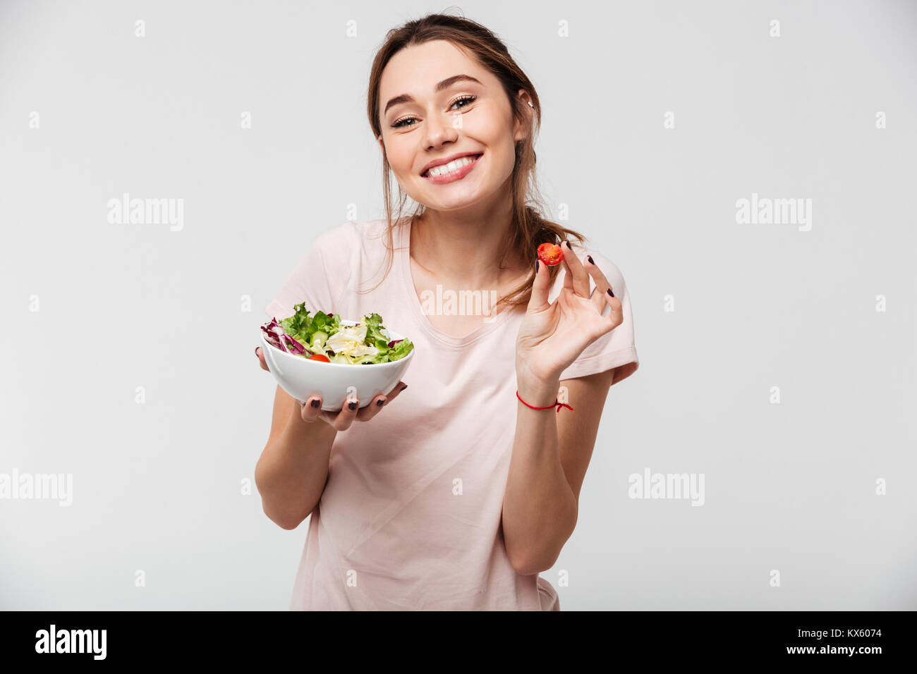 Portrait of a smiling cute girl showing fresh salad in a bowl isolated ...