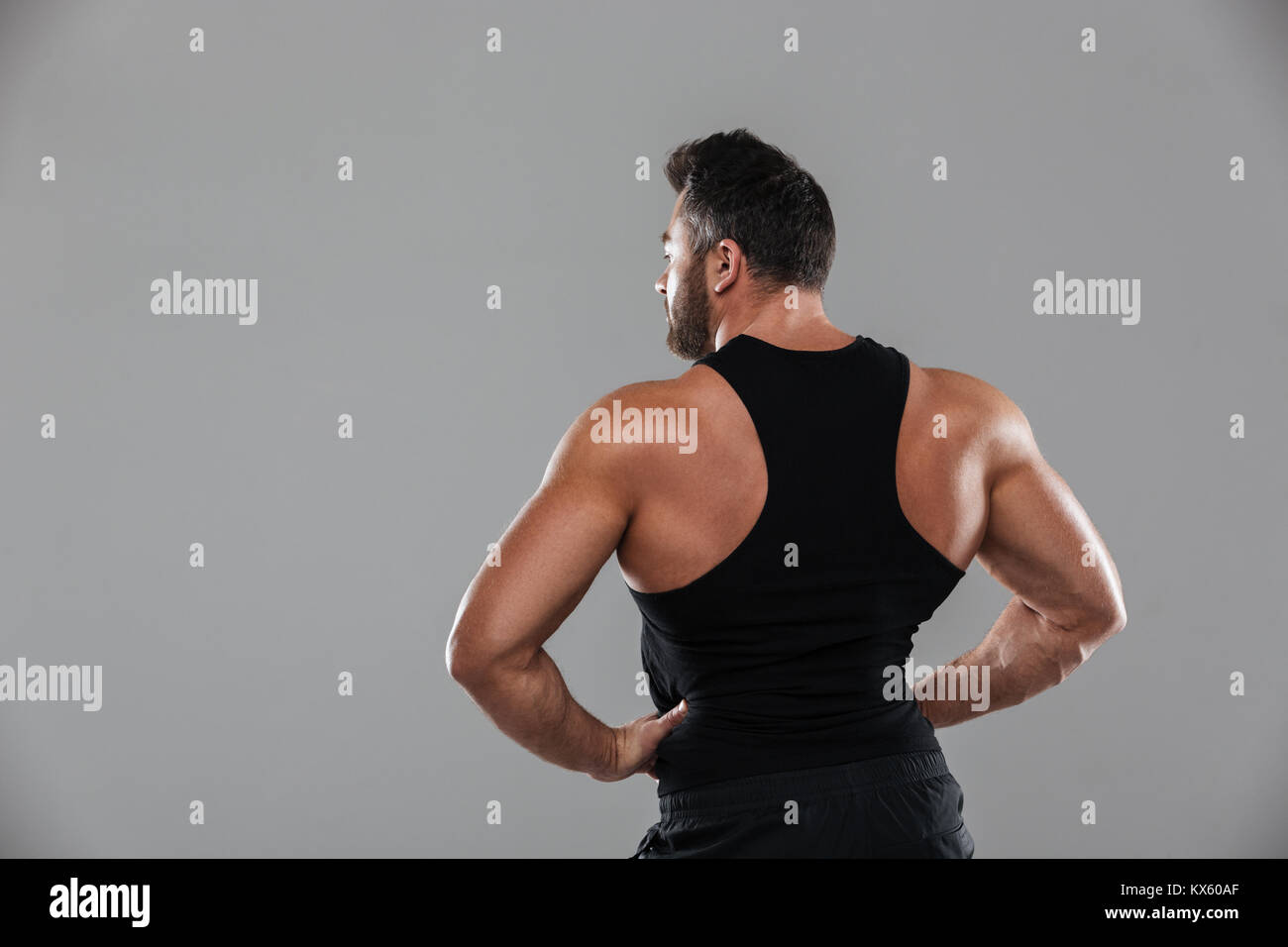 Back view of a muscular strong male bodybuilder standing with arms on ...