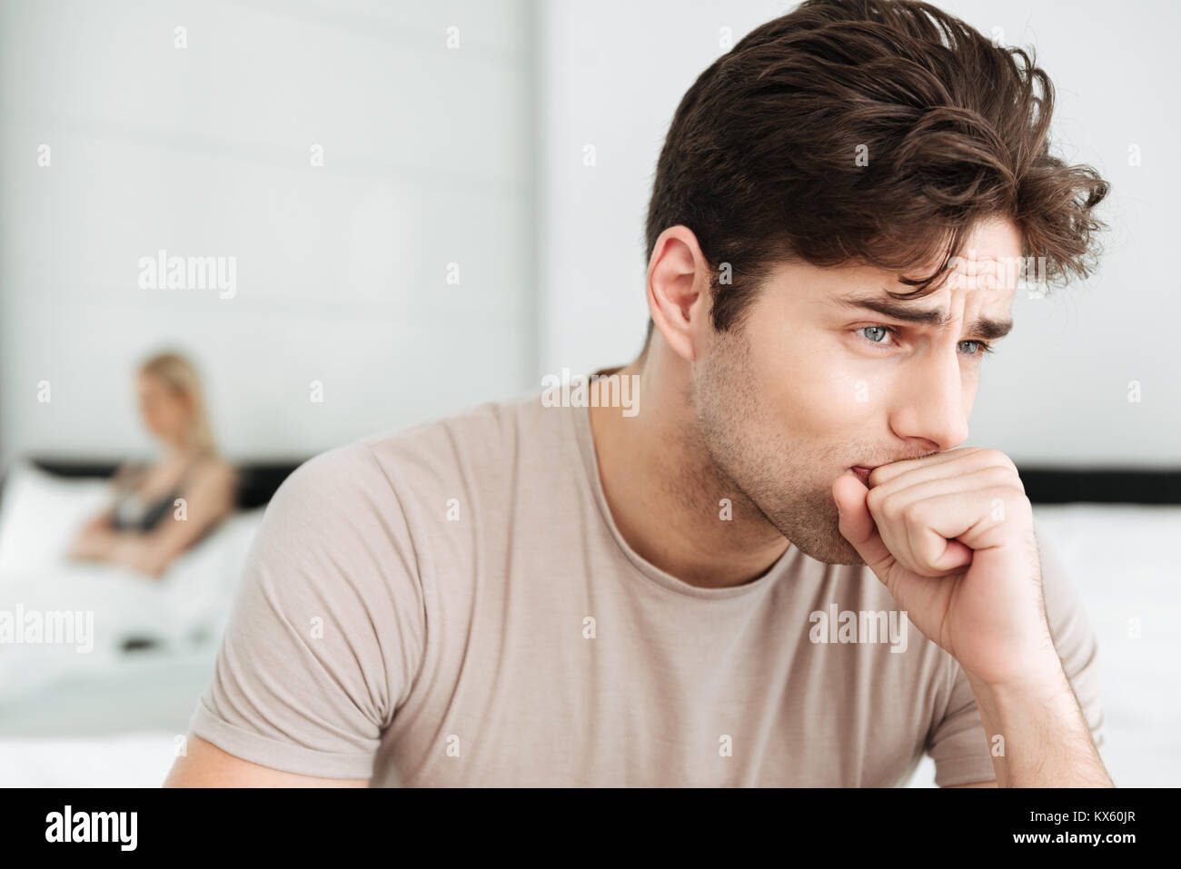 Portrait of sad brunette man in casual clothes sitting in bed at home ...