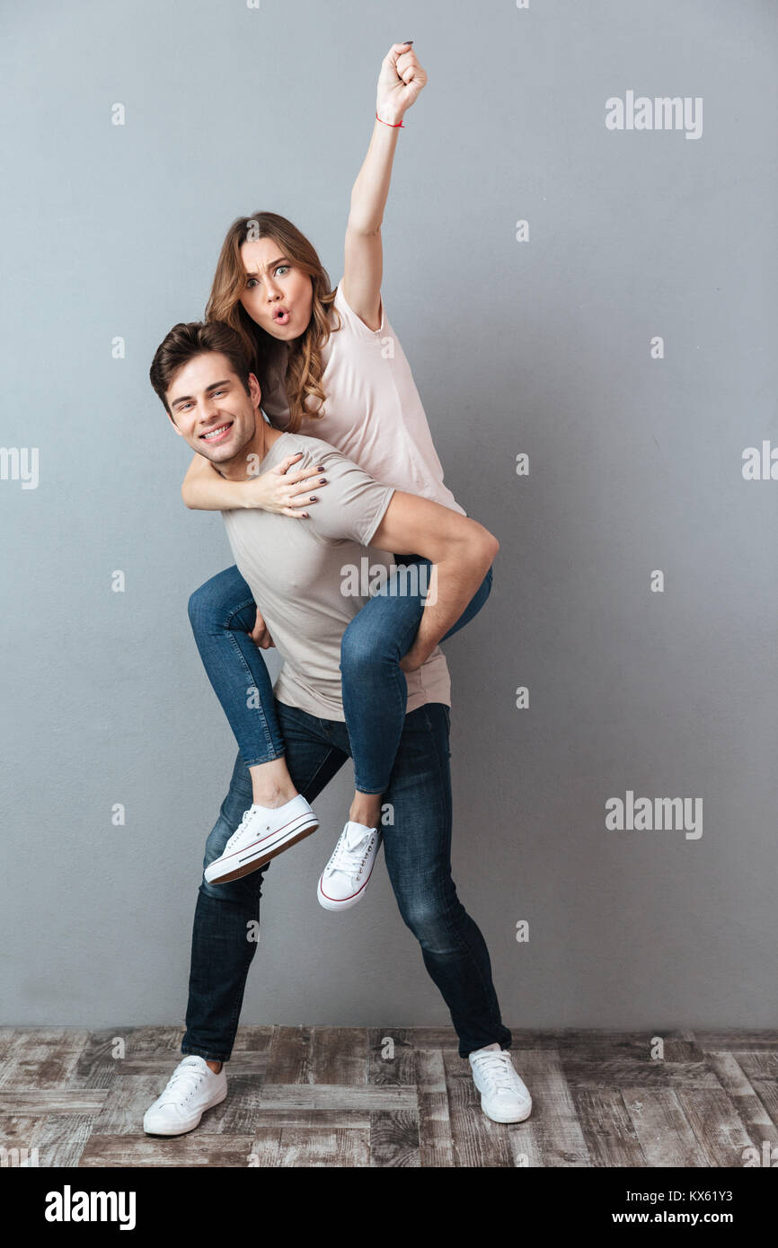 Full length portrait of a joyful man carrying girlfriend on his back ...