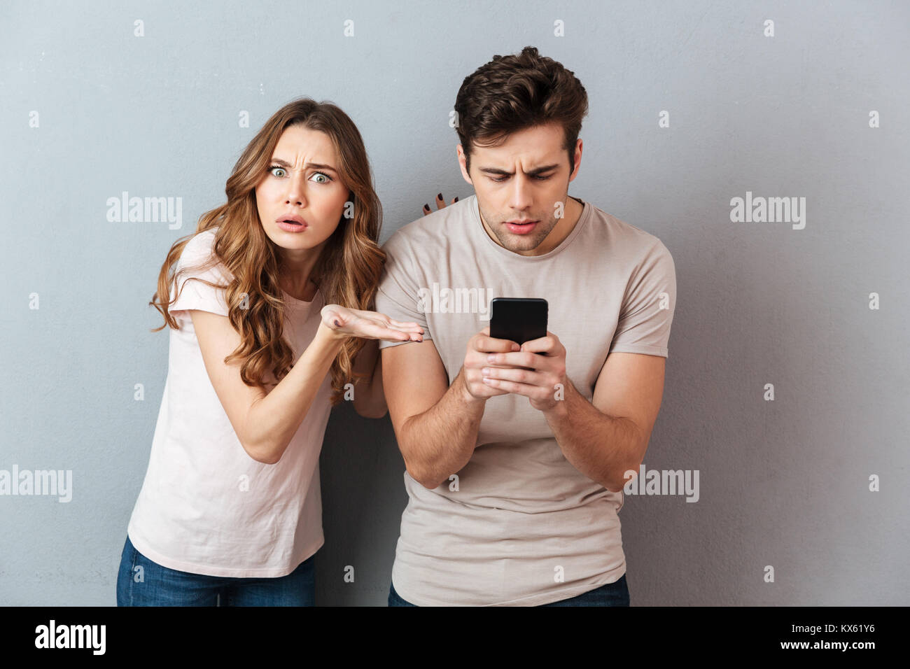 Portrait of a young couple standing with mobile phone, man is using ...