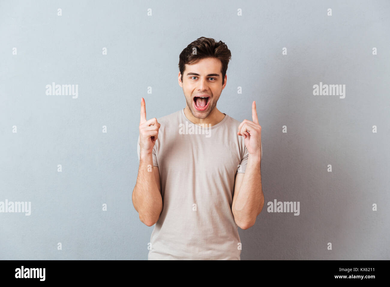 Portrait of a joyful happy man pointing fingers up and looking at ...