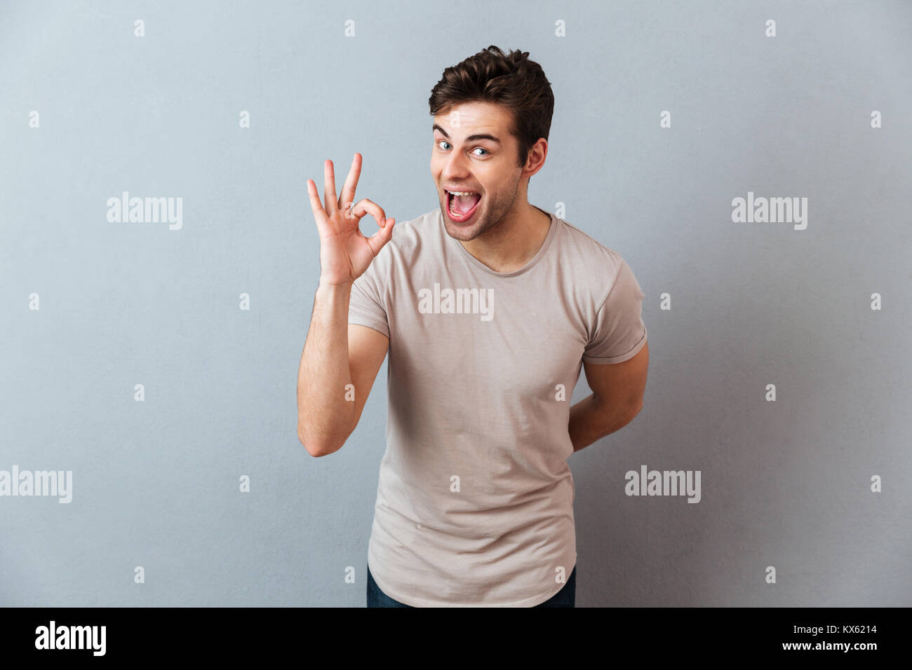 Portrait of a smiling happy man showing ok gesture isolated over gray ...