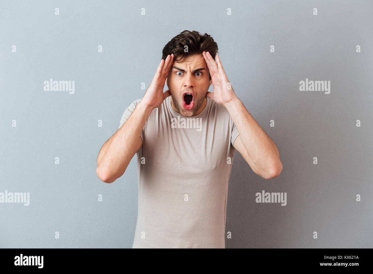 Portrait of an upset angry man holding hands at his face and shouting ...