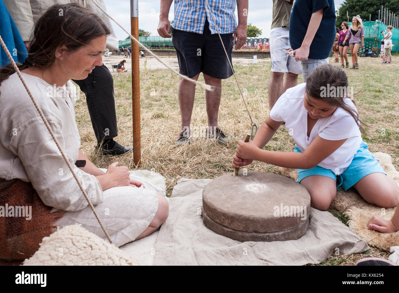 Young girl using a hand operated millstone at an archaeological dig ...