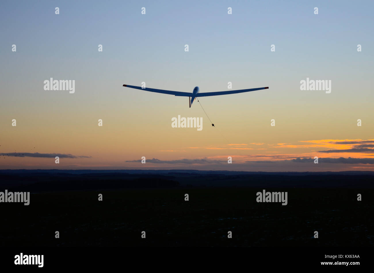 A glider is launched into the sunset, with dark ground below and the ...