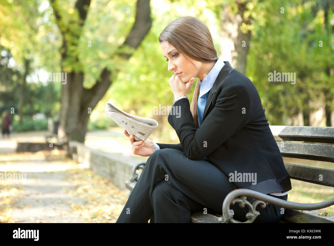 young thinking businesswoman reading newspaper , sitting on bench in ...