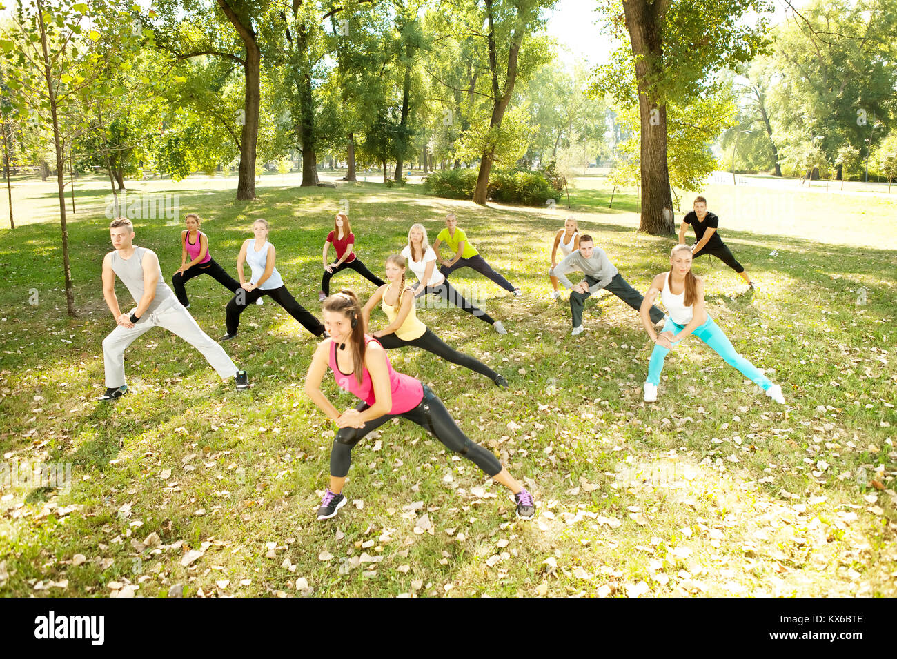 group of young people having aerobics class in park with instructor ...