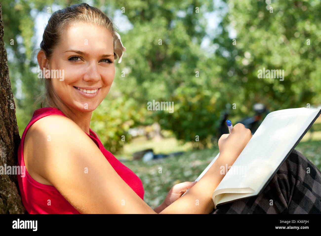 smiling girl sitting and writing in notebook outdoor Stock Photo - Alamy