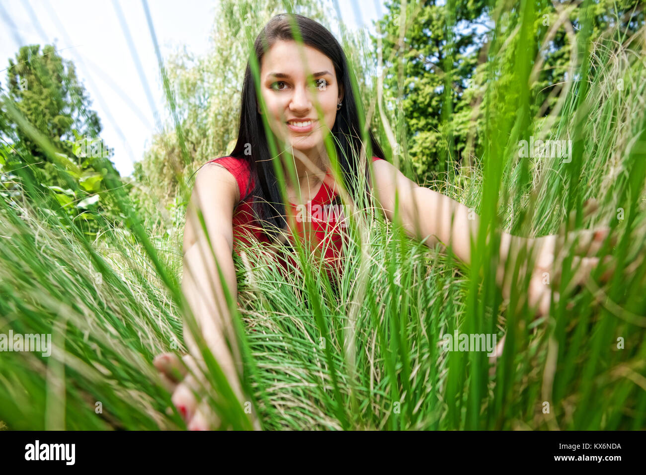 Young woman in a field peering through the long grass, looking at ...