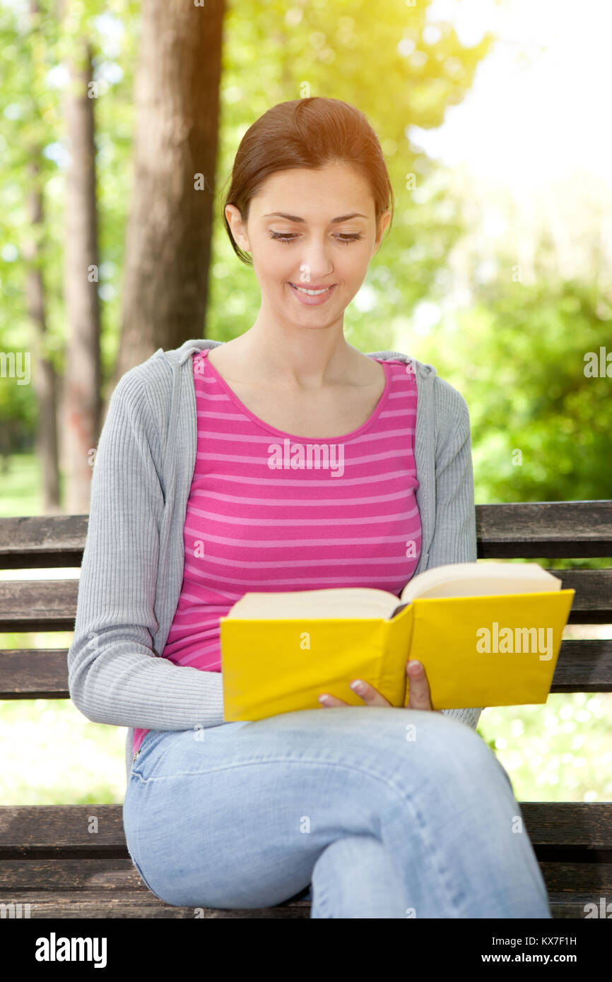 smiling girl on bench in park with book in hands Stock Photo - Alamy