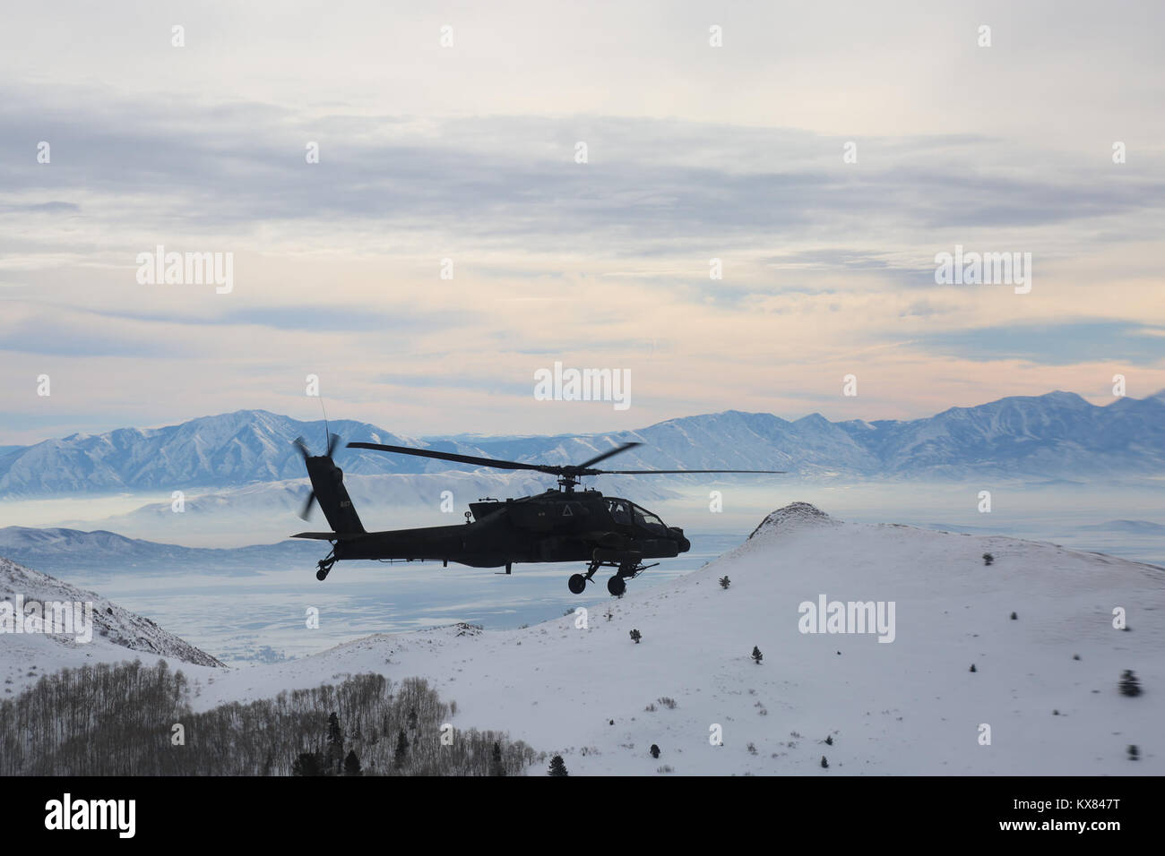 US Army National Guard flying AH-64 Apache military helicopter in snowy winter mountains Stock ...