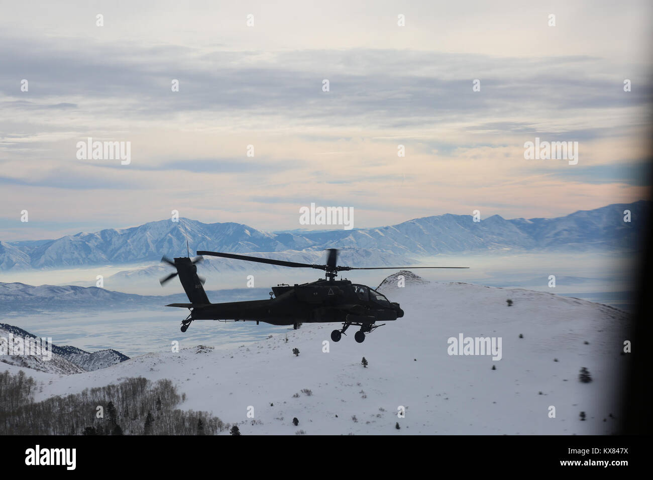 US Army National Guard flying AH-64 Apache military helicopter in snowy winter mountains Stock ...