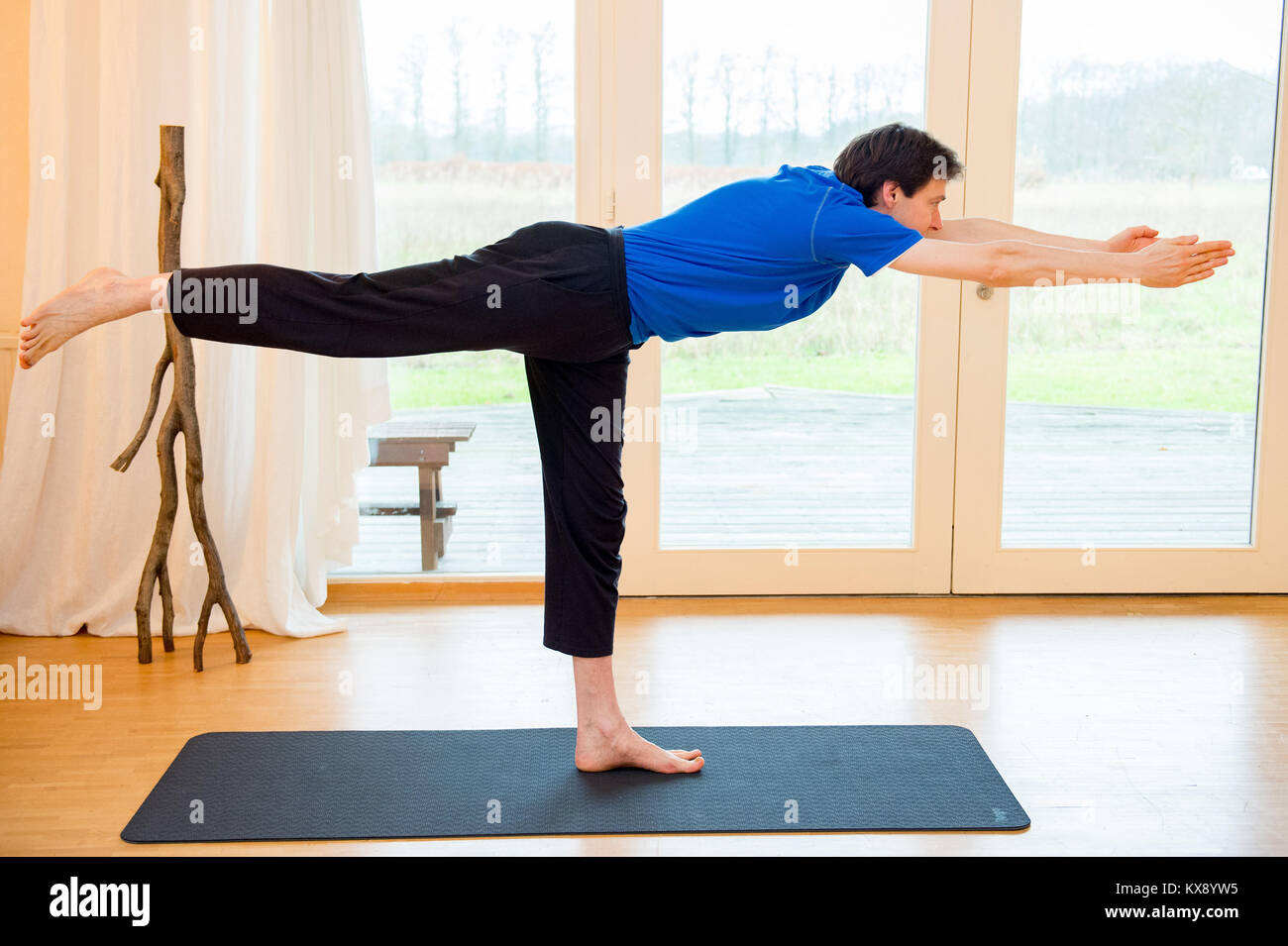 Man practicing yoga indoors in a retreat space doing Warrior 3 pose ...