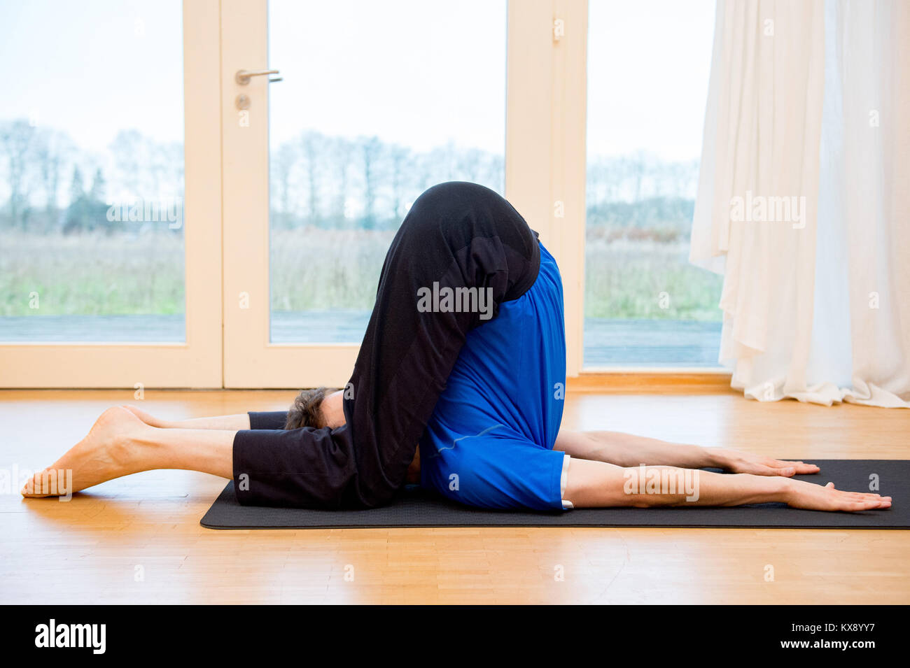 Man practicing yoga indoors in a retreat space doing Deaf Man's Pose ...