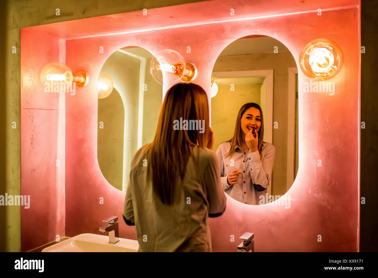 The woman paints lips in the toilet. Attractive happy woman paints lips ...
