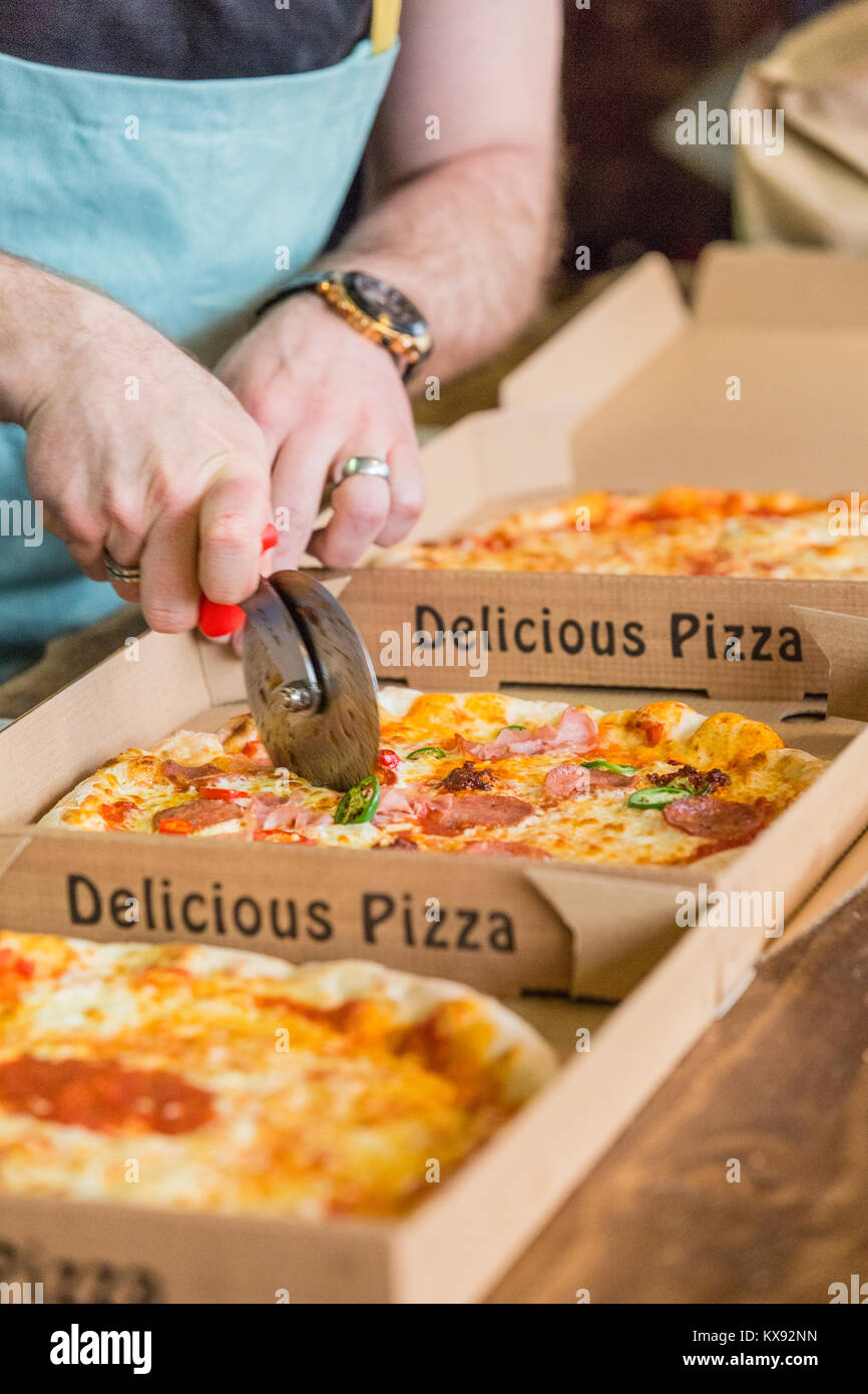 Freshly baked Pizza being cut in Pizza box ready for take away delivery ...