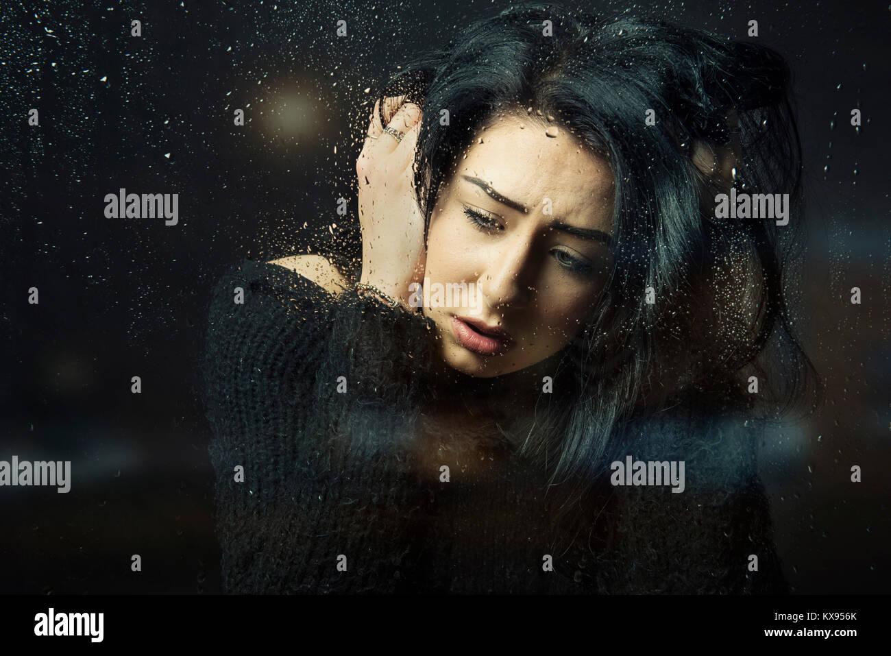 Woman sad depressed looking down hand on head sitting at rainy window ...